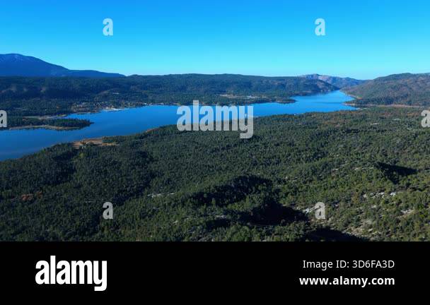 Aerial drone view of a wide mountain lake surrounded by dense evergreen ...