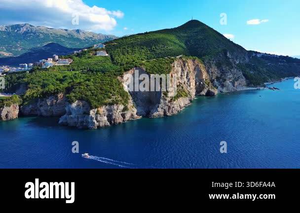 Rocky cliff with wild green vegetation above the waves of the shallow ...