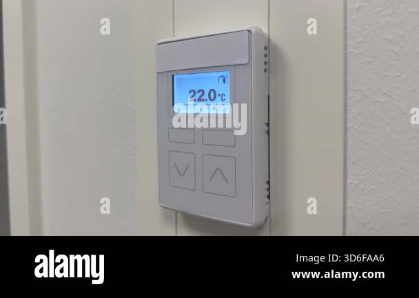 A modern digital smart thermostat mounted on a wall, displaying active ...