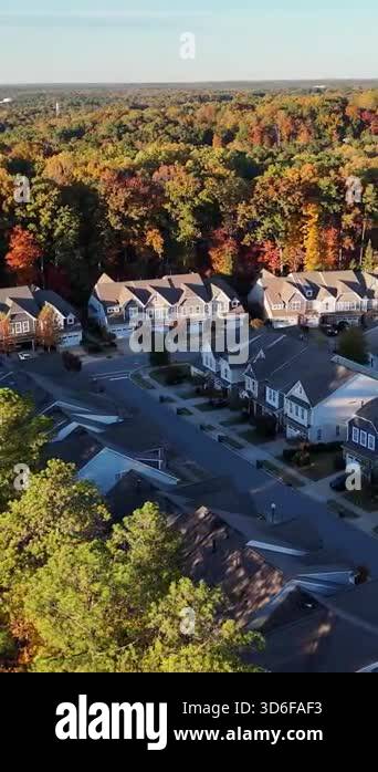 Drone footage showing a long suburban street lined with colorful trees ...