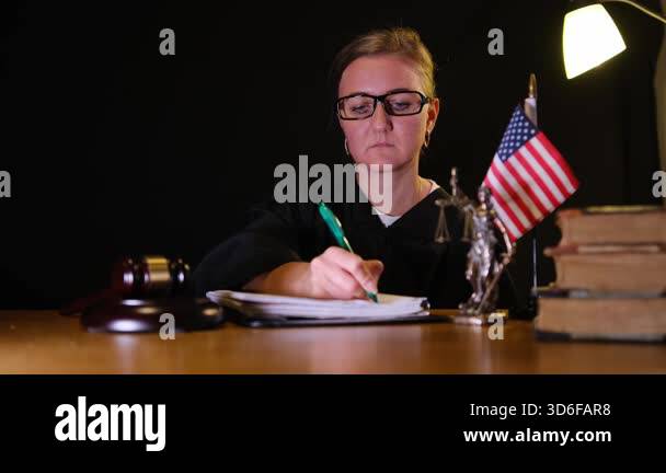 Female judge in dark robe writing notes at a desk with a gavel, justice ...