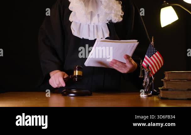 Judge in formal robe holding a legal document at the desk with gavel ...