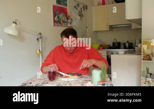 white man at kitchen table cutting into meal, home cook sampling dish ...