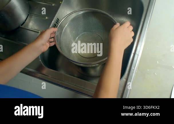 hands washing metal sieve under tap water, rinsing residue from ...