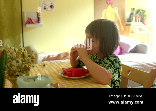 Young Asian girl indulges in fresh fruit, Child seated at sunlit ...