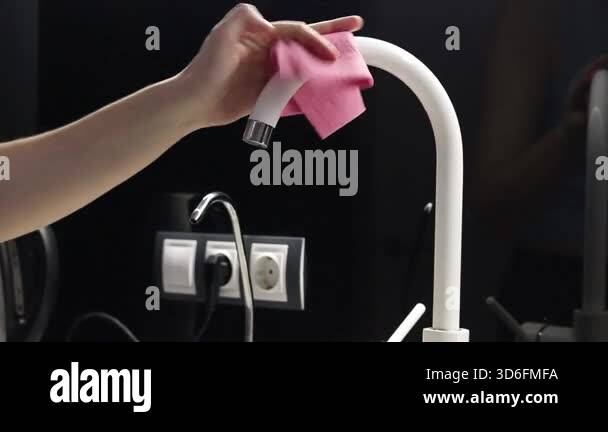 Wiping the kitchen faucet from dirt. Close-up of female hands wiping ...