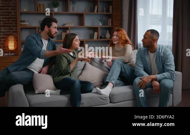 Multiracial four friends at home party talking on couch emotional ...