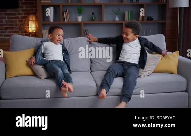 Two African American little boys jump falling on couch children ...