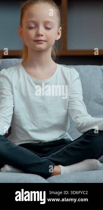 Caucasian calm child girl meditation at home in lotus position on couch ...