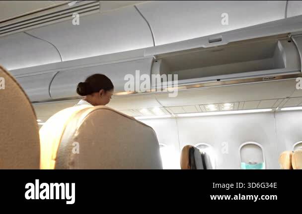Flight attendant in uniform reaches to adjust an overhead panel inside ...