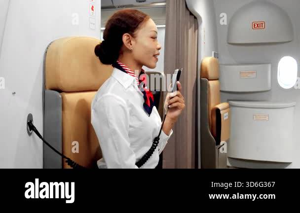 Smiling flight attendant on an airplane jumpseat speaks into a cabin ...
