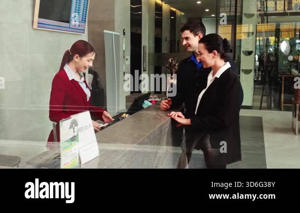 Hotel front desk receptionist assists arriving guests with check-in ...