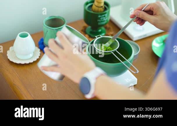 Hands sifting bright green Matcha powder into a bowl, preparing a ...