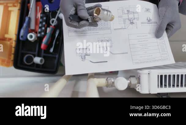 Male technician hands hold ball valve above schematic sheet reviewing ...