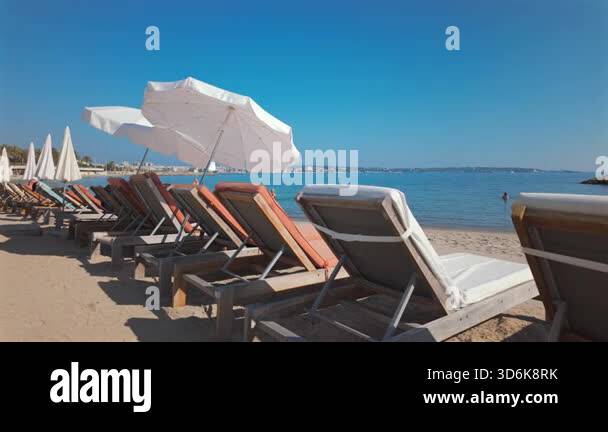 Row of empty sun loungers with white umbrellas on a sandy beach by the ...