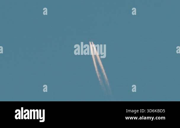 Airplane flying high above leaving long contrails in a clear blue sky ...