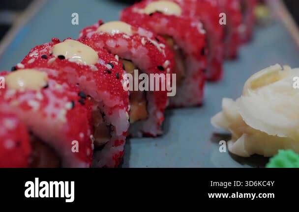 Close up of vibrant red sushi rolls topped with creamy sauce and sesame ...