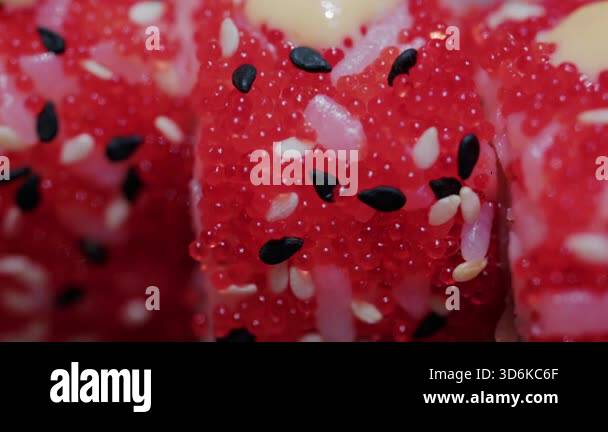 Close up of vibrant red sushi rolls topped with creamy sauce and sesame ...