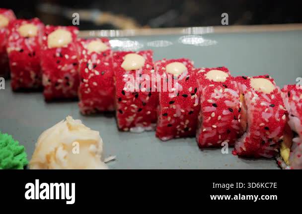 Close up of vibrant red sushi rolls topped with creamy sauce and sesame ...