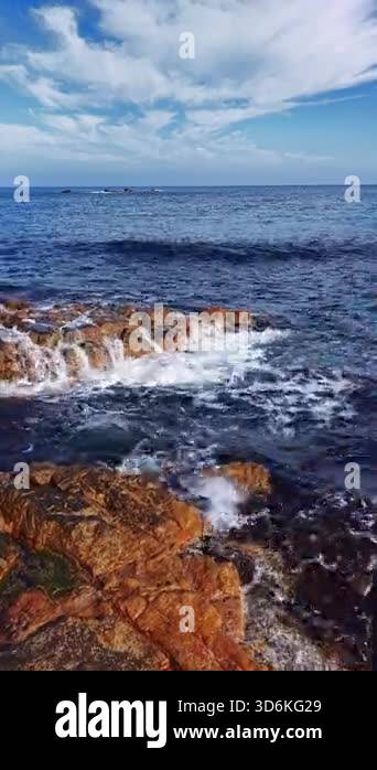 Ocean waves roll onto a rugged coastline, splashing against weathered ...