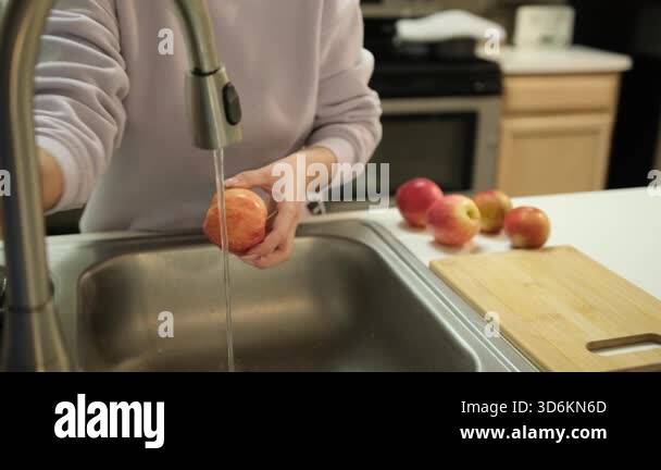 Woman washing apples under tap water in modern kitchen, fresh fruits on ...