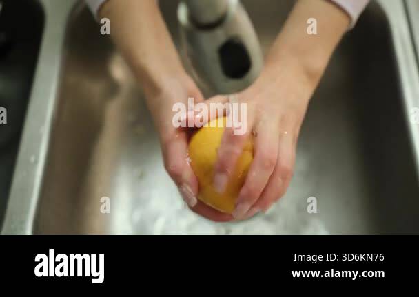 Woman washing orange with water from the kitchen. Peeling orange before ...