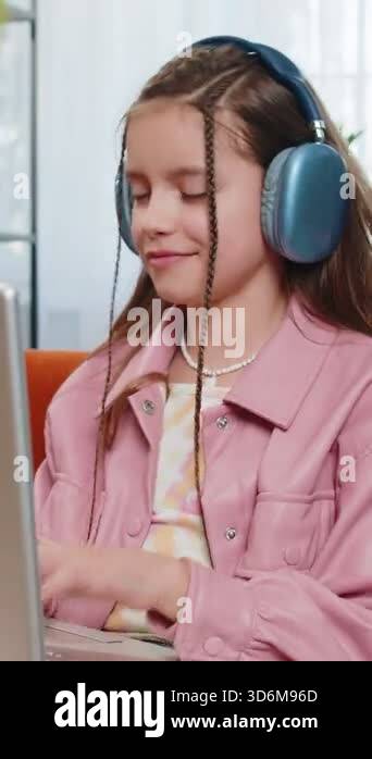 Caucasian preteen girl in headphones using laptop listens to music or ...