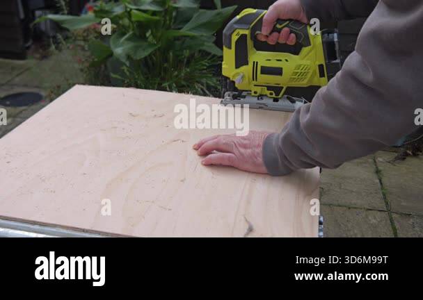 Close Up side view of a man using a battery powered Jigsaw cutting a ...