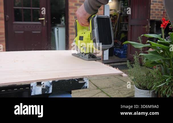 Rear view of a craftsman using a battery powered Jigsaw cutting a board ...