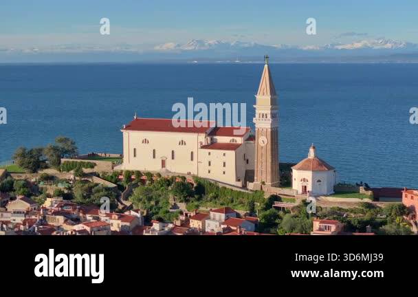 Aerial view of Piran with St. George Church and snowy Alps on ...