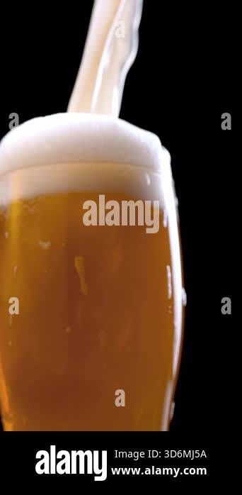 Frothy beer overfilling glass closeup with golden glow and spilling ...