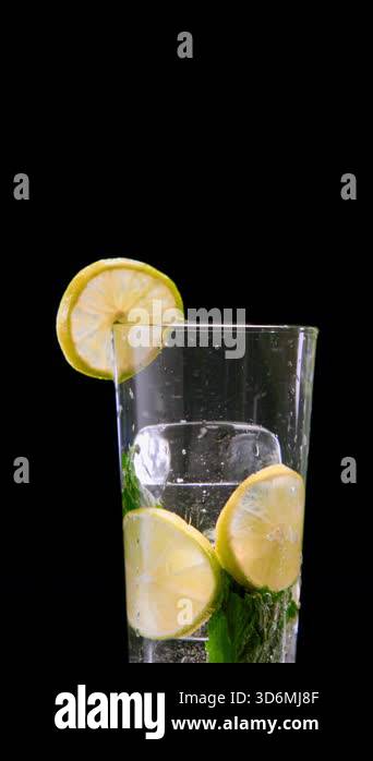 Zoom out lemon slice falling into sparkling drink on black background ...