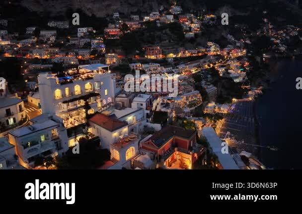 The town of Positano glows warmly at night. Houses and buildings are ...