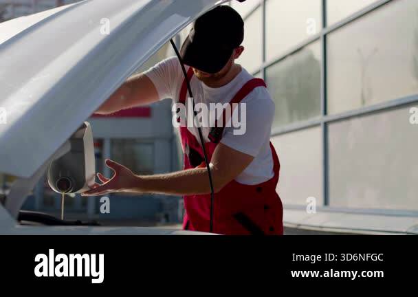 Mechanic in red overalls checks engine and fluid levels under the hood ...