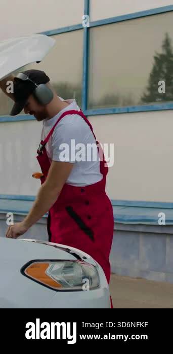 Mechanic in red overalls performs an under-the-hood check on a white ...