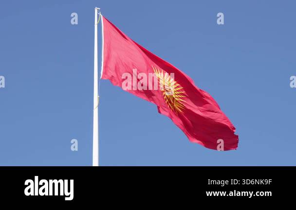 A red flag of Kyrgyzstan waving against a clear blue sky. The flag ...