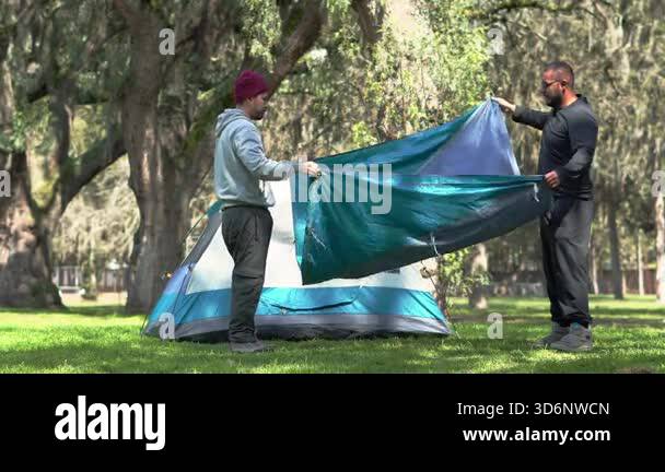 Two men work together folding a camping tent tarp and placing it into a ...