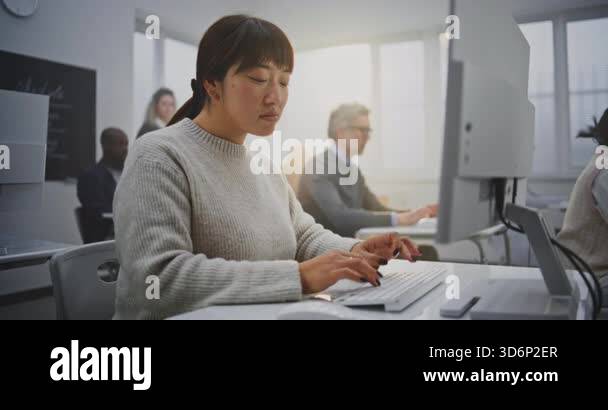 Smiling East Asian Woman in Modern Computer Classroom Focuses on Coding Project. Student Looks ...