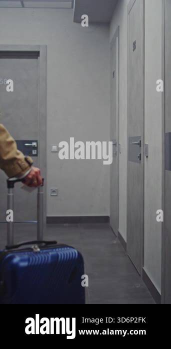 Traveler Woman in Trench Coat Rolls Luggage Down Hotel Hallway. Calmly ...