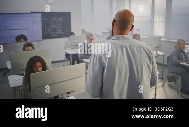 Professional Male Instructor Stands in Front of Adult Students in Computer Lab, Explaining ...