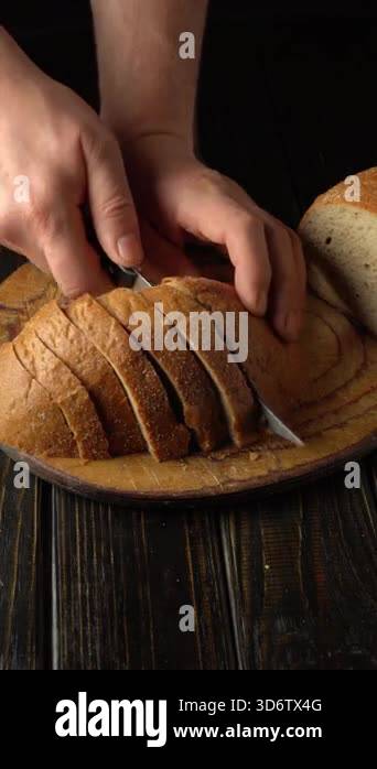 Hands are skillfully slicing a loaf of freshly baked bread on a wooden ...