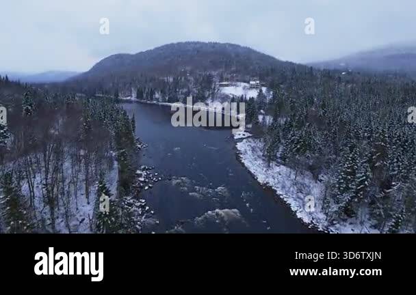Aerial cinematic shot of a winter river surrounded by snowy pine slopes ...