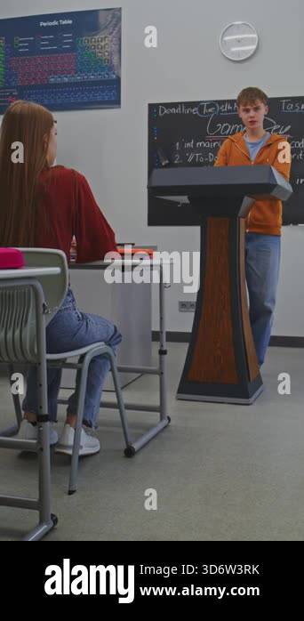Student in Orange Hoodie Stands Behind Podium in Front of Classmates ...