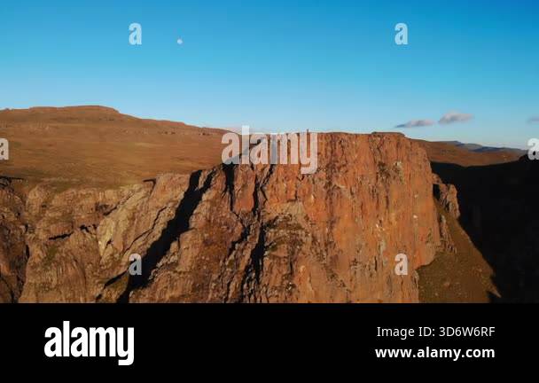 sunlit escarpment showing orange strata and steep drop, textured rock ...