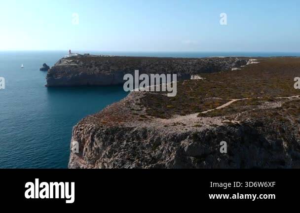 low rocky promontory with distant lighthouse, aerial glide shows ...
