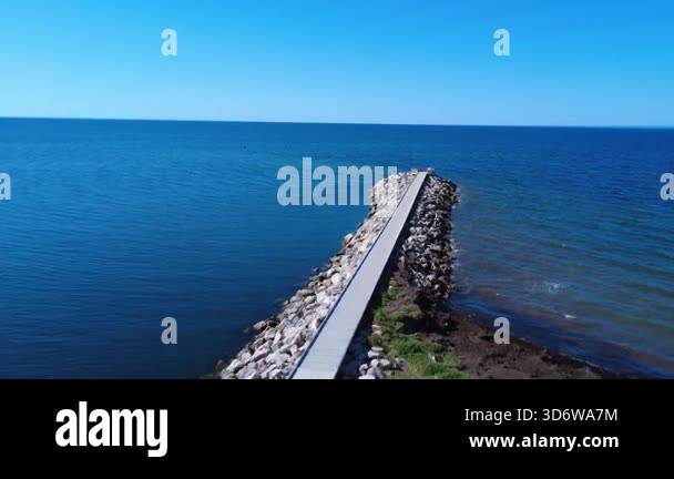 A sturdy wooden pier juts out through the waves into a calm blue ocean ...