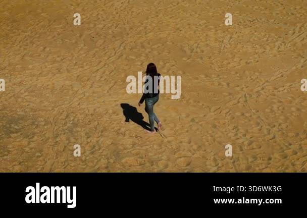 Woman walking barefoot across dry textured sand on sunny day. Female ...