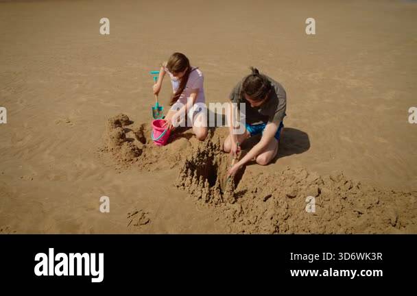 Brother and sister building big sandcastle with shovels and bucket ...