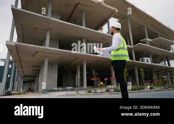 Male architect wearing a hard hat and safety vest standing in front of ...