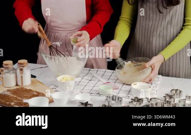Two women baking cookies together as one whisks flour, other mixes ...